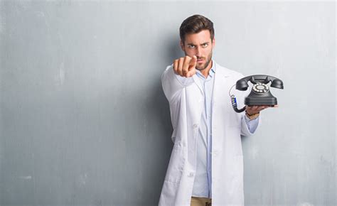 당신에 게 카메라를 손가락으로 가리키는 빈티지 전화를 들고 회색 그런 지 벽에 잘생긴 젊은 전문 남자 손 기호 앞에서 긍정적이