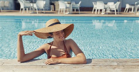 모자를 쓴 아름다운 평온한 여자는 수영장에서 휴식을 취하고 열대 리조트에서 여름 휴가를 즐기고 있습니다 수영장 가장자리에서 일광욕을 하는 행복한 젊은 여성의 초상화 여행