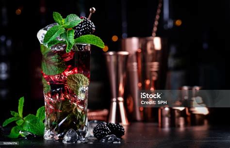 화이트 럼 시럽 소다 라임 베리 민트 얼음이 담긴 블랙베리 모히토 알코올 칵테일 음료 어두운 바 카운터 배경 바 도구 및 병