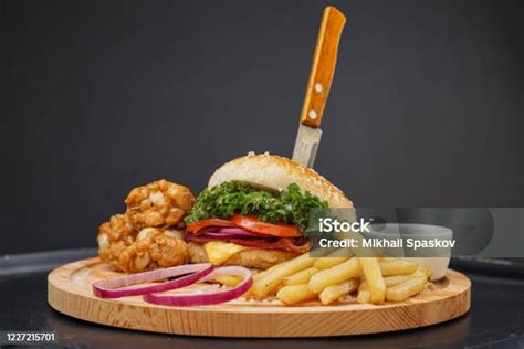 패스트 푸드의 콤보 세트 육즙이 많은 햄버거 감자 튀김 닭 다리와 소스 검은 색 배경에 나무 보드와 칼붙이 제공 패스트 푸드