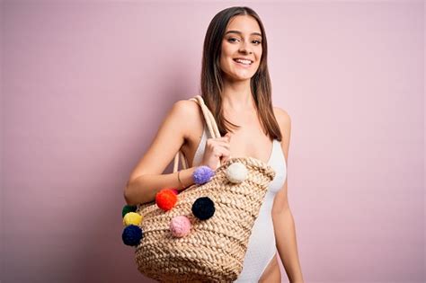 젊은 아름다운 갈색 머리 여자 휴가 에 착용 화이트 수영복 들고 여름 가방 과 행복한 얼굴 서서 치아를 보여주는 자신감 미소와 미소 젊은 여자에 대한 스톡 사진 및 기타