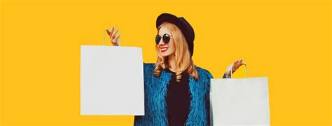 파란색 모피 코트 검은색 둥근 모자 선글라스를 쓴 쇼핑백을 들고 노란색 배경에 포즈를 취하는 아름다운 세련된 웃는 여성의 초상화 인조 모피에 대한 스톡 사진 및 기타 이미지