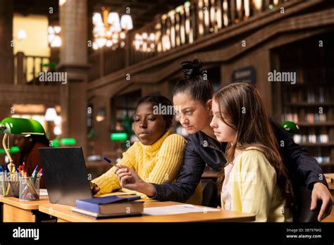 Caucasian Tutor Guiding Two Elementary School Girls At A Library Desk Providing Private Lessons