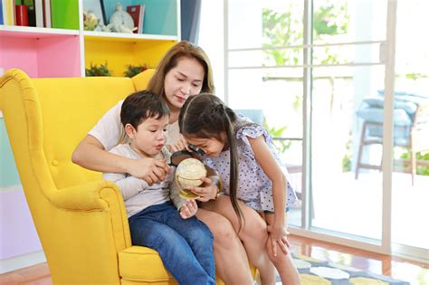 행복 한 아시아 미혼모 아이 딸과 아들 앉아 소파에 소파에 앉아 화려한 현대 거실 와 미소 얼굴 동안 재생 하는 돋보기 와 지구