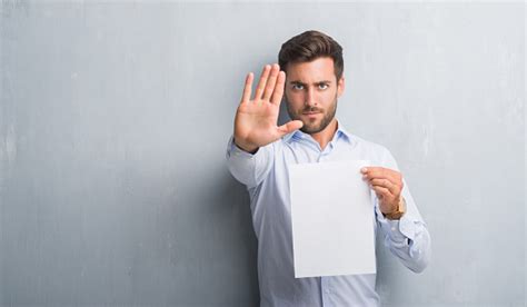 그런 지 회색 벽 잡고 빈 종이 시트에 잘생긴 젊은 남자 오픈 손으로 하 고 심각 하 고 자신감 표현 방어 제스처와 정지 신호 계약 경계 표지에 대한 스톡 사진 및 기타