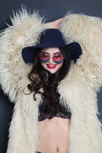 밝은 메이크업과 긴 웨이브 머리를 가진 행복 한 젊은 성인 여성 패션 모델 파란색 모자와 선글라스를 착용 푸른 스튜디오 벽