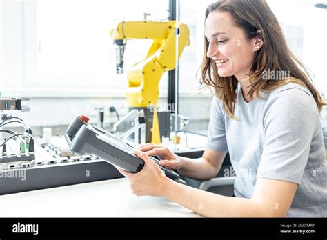 female skilled worker in robotic factory controlling robot arm with