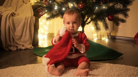 산타클로스 의상을 입은 귀여운 웃는 어린 소년이 거실에 장식된 크리스마스 트리 아래에 앉아 있다 겨울 방학을 축하하는 가족과 아이들 아파트에 대한 스톡 사진 및 기타 이미지