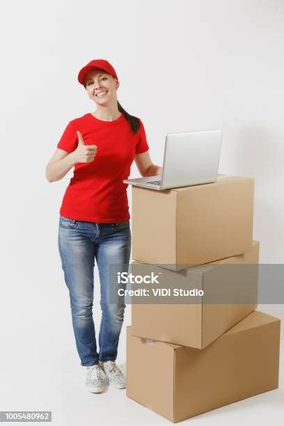 전체 길이 빨간 모자에 배달 젊은 여자의 초상화 T셔츠는 흰색 배경에 고립 여성 택배 노트북 Pc 컴퓨터와 빈 골 판지 상자 근처에 서 수신 패키지입니다 공간 복사 가냘픈에