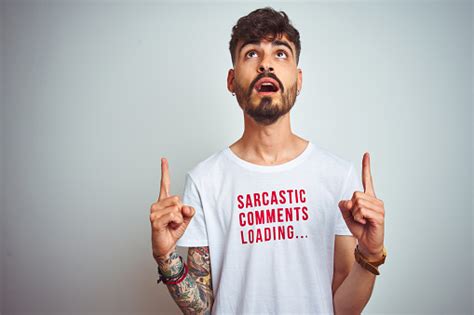 고립 된 흰색 배경 위에 서있는 멋진 티셔츠를 입은 문신을 한 청년은 손가락과 팔을 들고 위를 올려다 보고 놀랐습니다 T 셔츠에 대한 스톡 사진 및 기타 이미지 Istock