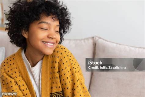 아프리카 헤어스타일을 한 아름다운 아프리카계 미국인 소녀가 집 실내 소파에 앉아 웃고 있다 곱슬머리를 가진 젊은 아프리카 여자가 웃고 있다 자유 행복 평온 행복한 사람들의