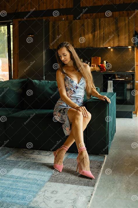Woman In Floral Dress Sitting On Sofa And Looking At Heel Of Her New
