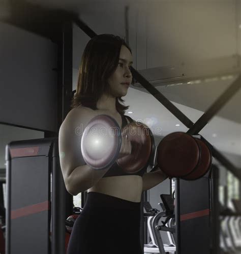 Young Lady With Fit And Firm Body Lifting Dumbbell Exercising In Gym