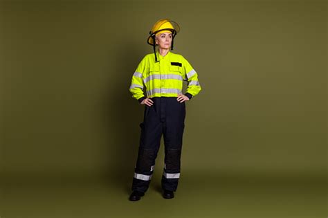 눈에 잘 띄는 유니폼을 입은 자신감 넘치는 여성 엔지니어가 카키색 배경에 보호 헬멧과 작업복을 입고 서 있습니다 55 59세에 대한 스톡 사진 및 기타 이미지 Istock