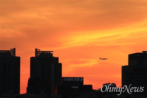붉은 노을을 배경으로 서 있는 빌딩들 그 사이로 비행 오마이포토