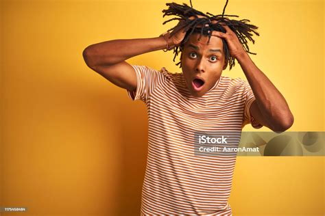 고립 된 노란색 배경 미친 위에 서 줄무늬 티셔츠를 입고 공포를 가진 아프로 남자 미친 머리에 손을 무서워 두려워하고 열린 입으로 충격의 놀라움 T 셔츠에 대한 스톡 사진