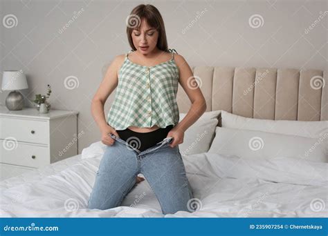 Young Woman Trying To Squeeze Into Tight Jeans On Bed At Home Space
