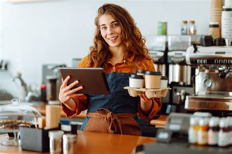 곱슬 머리와 태블릿을 손에 들고 커피 숍의 잘 생긴 젊은 매니저는 커피 숍에서 테이크 아웃 커피를 제공합니다 테이크 아웃 음식
