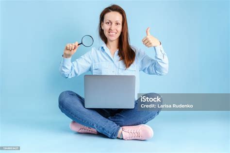 인터넷에서 온라인 쇼핑 제품 검색 젊은 성인 소녀가 그녀의 무릎에 노트북과 함께 앉아 파란색 배경에 그녀의 손에 돋보기를 들고 30 39세에 대한 스톡 사진 및 기타 이미지