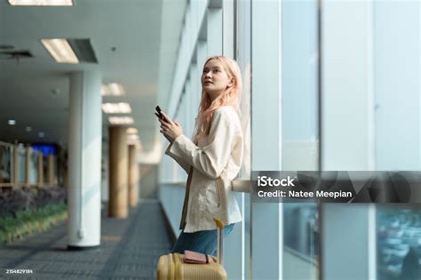 공항 터미널에서 스마트폰을 사용하는 여행 가방을 든 젊은 여성 현대 여행 컨셉 캐주얼 복장 비행 대기 Brand Name Smart Phone에 대한 스톡 사진 및 기타