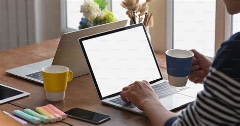 똑똑한 남자가 사무 기기로 둘러싸인 나무 작업 책상을 얹고 흰색 빈 화면 컴퓨터 노트북에서 작업하면서 커피를 마시고 있습니다 사진 Unsplash의 테이블 이미지