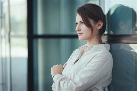 자신감 넘치는 아름다운 젊은 백인 여성이 유리 벽에 기대어 사무실 건물에 서서 의도적으로 옆을 바라 봅니다 30 34세에 대한