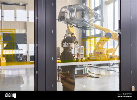 Engineer In A Modern Robotics Lab Working On Programming And Inspecting Robotic Arms Used For