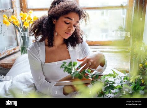 Pretty Romantic African American Girl Reading Book Sitting On Windowsill Suraunded With