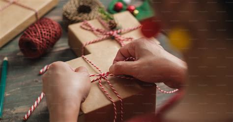 나무 테이블에 크리스마스 장식으로 뒤틀린 갈색 종이로 크리스마스 수제 선물 상자를 만드는 여자 사진 Unsplash의 묶인 활 이미지