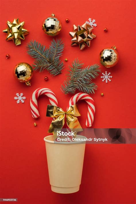 사탕 지팡이로 가득 찬 일회용 종이컵과 황금 크리스마스 트리 장난감으로 장식된 크리스마스 배경 커피 한 잔 개념입니다 빨간색 배경입니다 플랫 레이 금색에 대한 스톡 사진 및