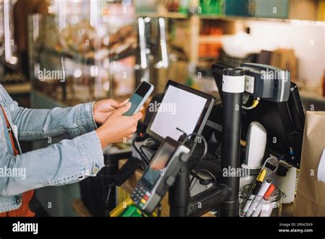 Midsection Of Woman Using Smart Phone While Scanning QR Code For Payment At Store Checkout Stock