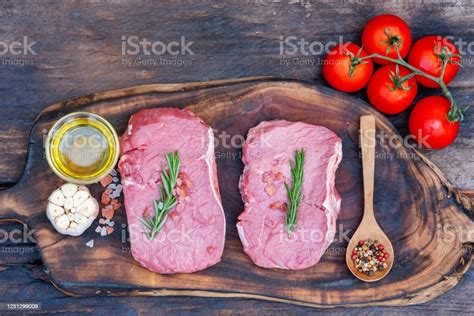로즈마리 소금 마늘 토마토 후추 올리브 오일이 있는 주방의 나무 보드 테이블에 생 고기 쇠고기 스테이크 유기농 신선한 재료 쇠고기 스테이크 생 고기 나무 접시에 고기 쇠고기