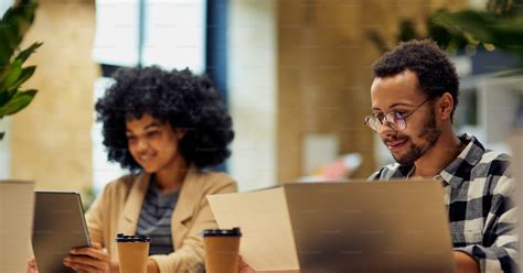 현대 기술 사용 두 명의 젊은 다인종 사업가가 책상에 앉아 코워킹 스페이스에서 함께 일하고 있습니다 사무실 생활 팀워크 및 비즈니스 사진 Unsplash의