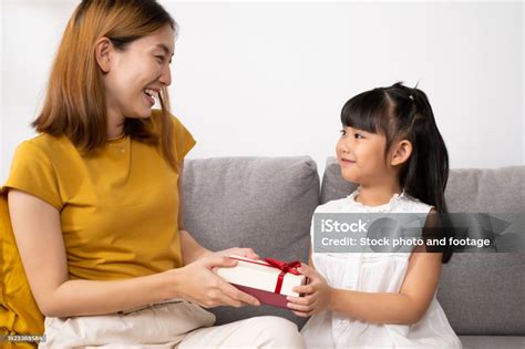 어린이 아시아 소녀는 거실 안에서 포옹하고 키스하기 전에 어머니를 놀라게하기 위해 선물을 숨 깁니다 여성 부모 가족 관계와의 행복한 순간 어머니의 날 아이에 대한 스톡 사진