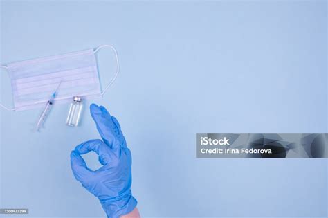 새로운 코로나바이러스에 대한 예방 접종 파란색 장갑을 낀 손은 병의 코로나바이러스 백신 접종 약물의 배경에 있는 Ok 기호와 파란색 배경의 주사기를 보여줍니다 40 44세에