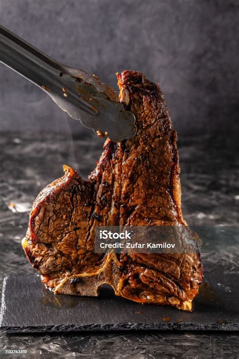 연기가 나는 큰 쇠고기 로스트 티 본 스테이크 검은 배경에 스테이크 고기 집게를 들고 머리 요리사 광자 이미지 복사 공간 검정색 배경에 대한 스톡 사진 및 기타 이미지