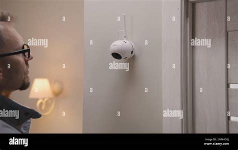 Installer In Uniform Puts Security Camera On Wall Fastening And Connects It To System With Cable