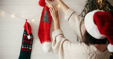 아늑한 스웨터를 입고 산타 모자를 쓴 세련된 소녀는 흰 벽에 스타킹 화환 조명 크리스마스 트리가 있는 크리스마스 휴일을