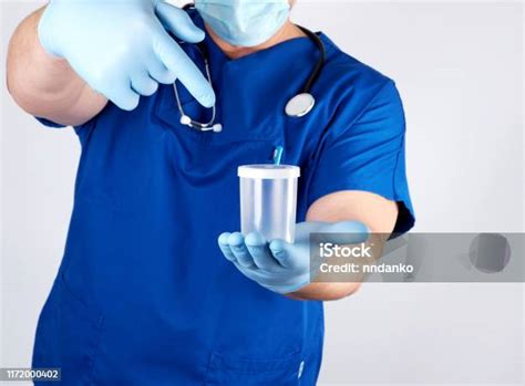 파란색 유니폼과 라텍스 장갑의 의사가 소변 샘플을 채취하기위한 빈 플라스틱 용기를 들고 있습니다 개념에 대한 스톡 사진 및 기타