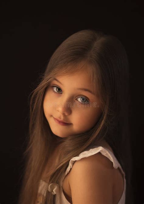 Portrait Of A Little Beautiful Girl With Long Hair Against A Dark