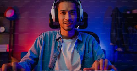 행복한 아시아 남자 게이머는 헤드폰 참여 놀이 비디오 게임 화려한 네온 불빛 컴퓨터 밤 현대 집에서 거실에 있습니다 E스포츠 스트리밍 게임 온라인 가정 격리 활동 개념