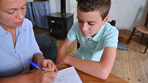 Mother Helping Her Son With Homework At The Kitchen Table Focusing On Schoolwork And Education