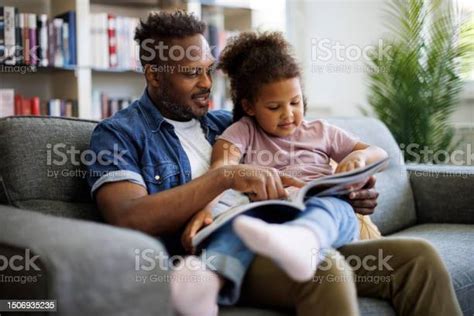 행복한 아프리카계 미국인 아버지와 사랑스러운 혼혈 딸이 집에서 함께 시간을 보내며 책을 읽고 웃고 있다 어린이 교육 및 발달 개념 잡지에 대한 스톡 사진 및 기타 이미지
