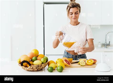Young woman pouring freshly squeezed homemade orange juice into the ...