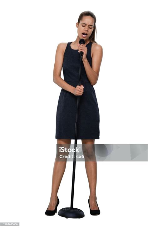 아프리카계 미국인 젊은 여성 가수가 비즈니스웨어를 입고 마이크 스탠드를 들고 사무실에서 흰색 배경 앞에서 춤을 추고 있습니다