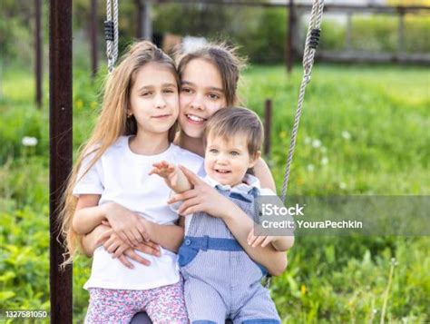 밝은 옷을 입은 쾌활한 아이들은 꽃이 만발한 녹색 집 정원에서 거리 스윙을 타고 행복한 미소로 웃습니다 3 명에 대한 스톡 사진 및 기타 이미지 Istock