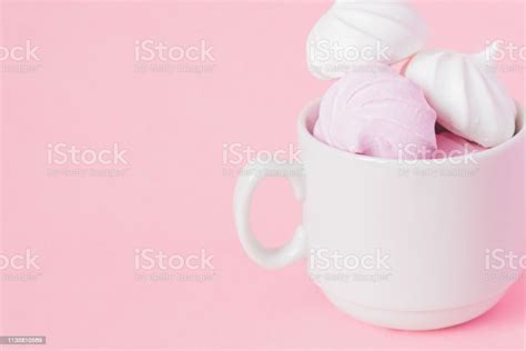 분홍색 배경에 작은 도자기 커피 컵에 흰색과 분홍색 트위스트 머 랭 설탕을 휘 핑 하 고 달걀 흰 자를 구워 만든 프렌치 디저트