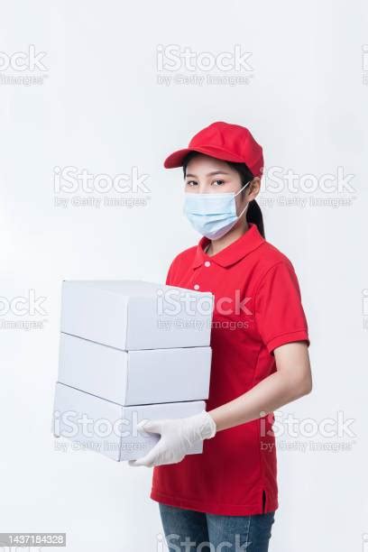 빨간 모자 빈 티셔츠 유니폼 얼굴 마스크 장갑을 낀 의식이 있는 젊은 배달원의 이미지는 밝은 회색 배경 스튜디오에 격리된 빈