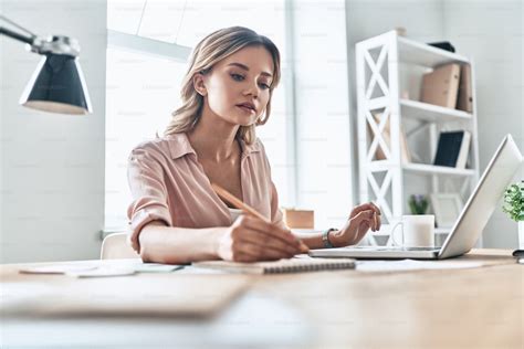 스마트 캐주얼 웨어를 입은 아름다운 젊은 여성이 현대적인 사무실에 앉아 무언가를 적고 있습니다 사진 Unsplash의 우크라이나 이미지