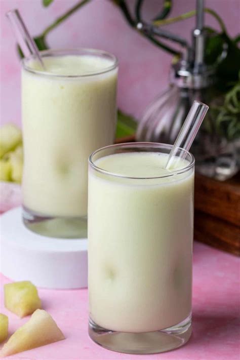 Two Glasses Of Honeydew Smoothie Are On A Pink Background With Plants
